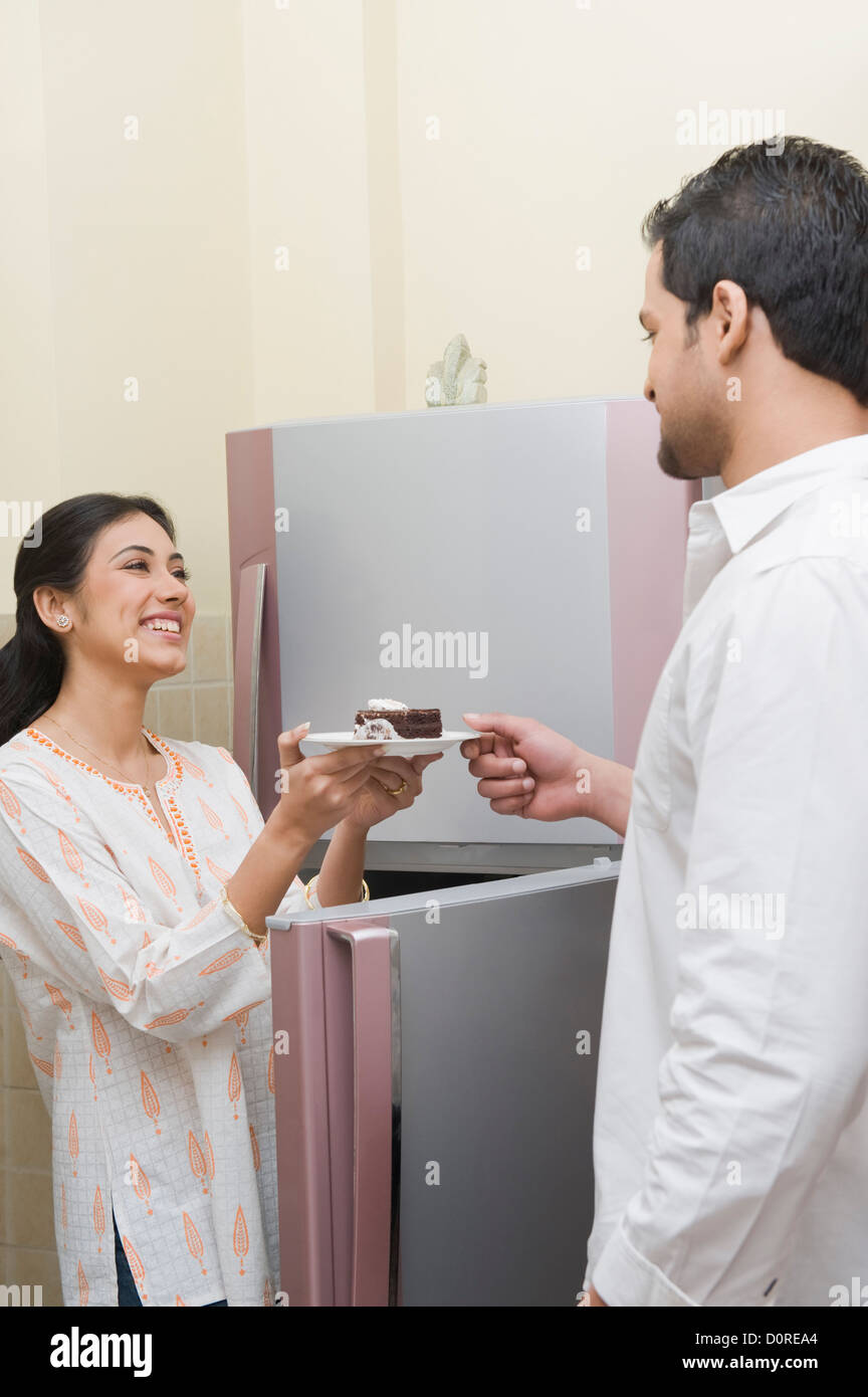 Woman giving a plate of cake to a man in front of a refrigerator Stock ...