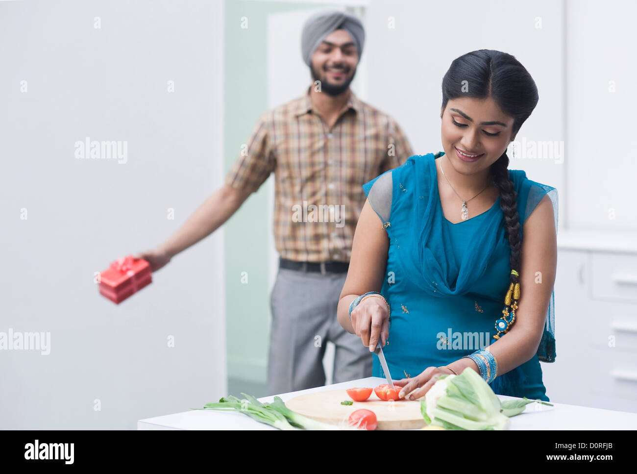 Woman chopping vegetables in the kitchen with her husband standing ...