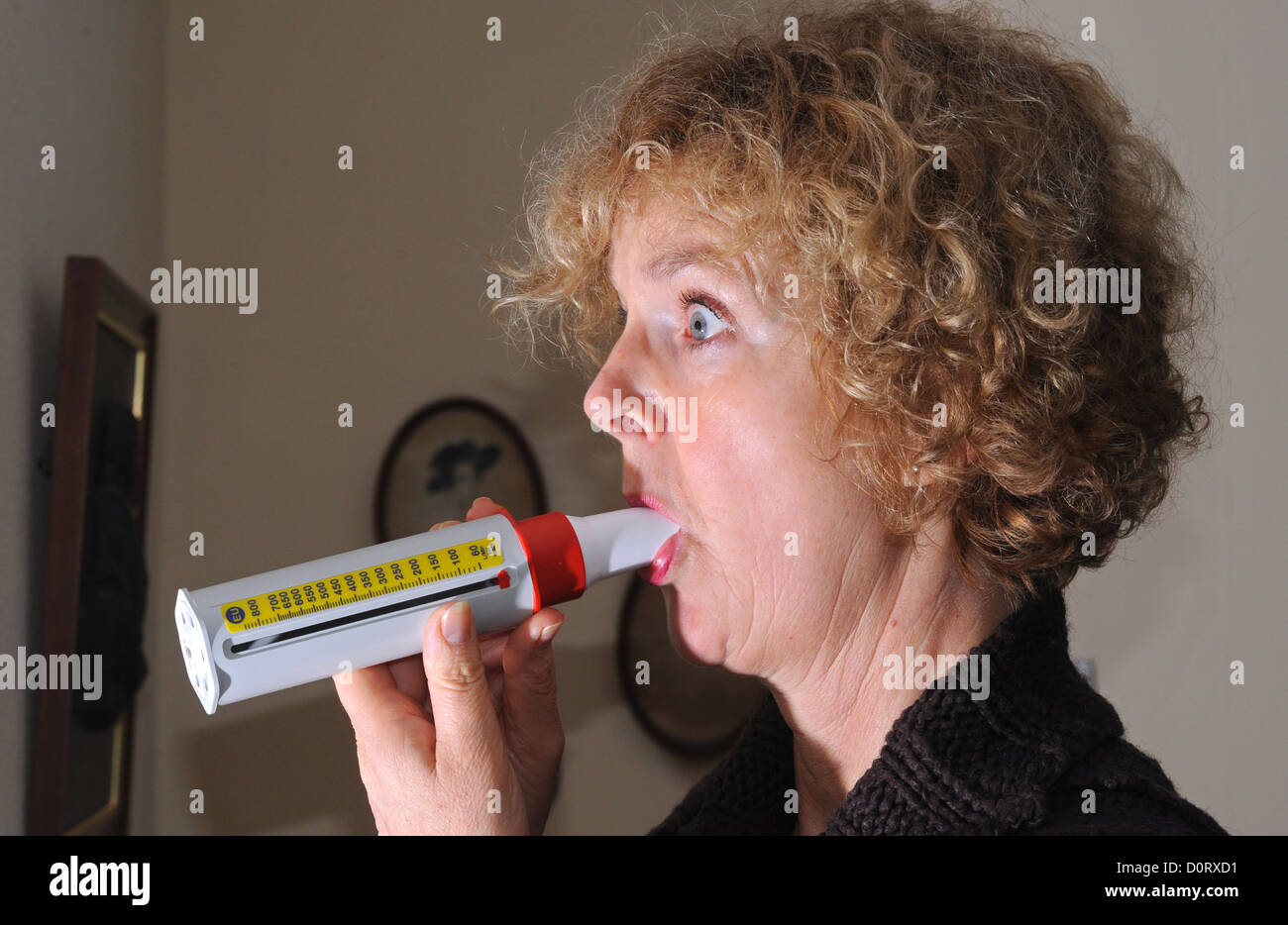 Middle aged female asthma sufferer blowing into a peak flow meter ...