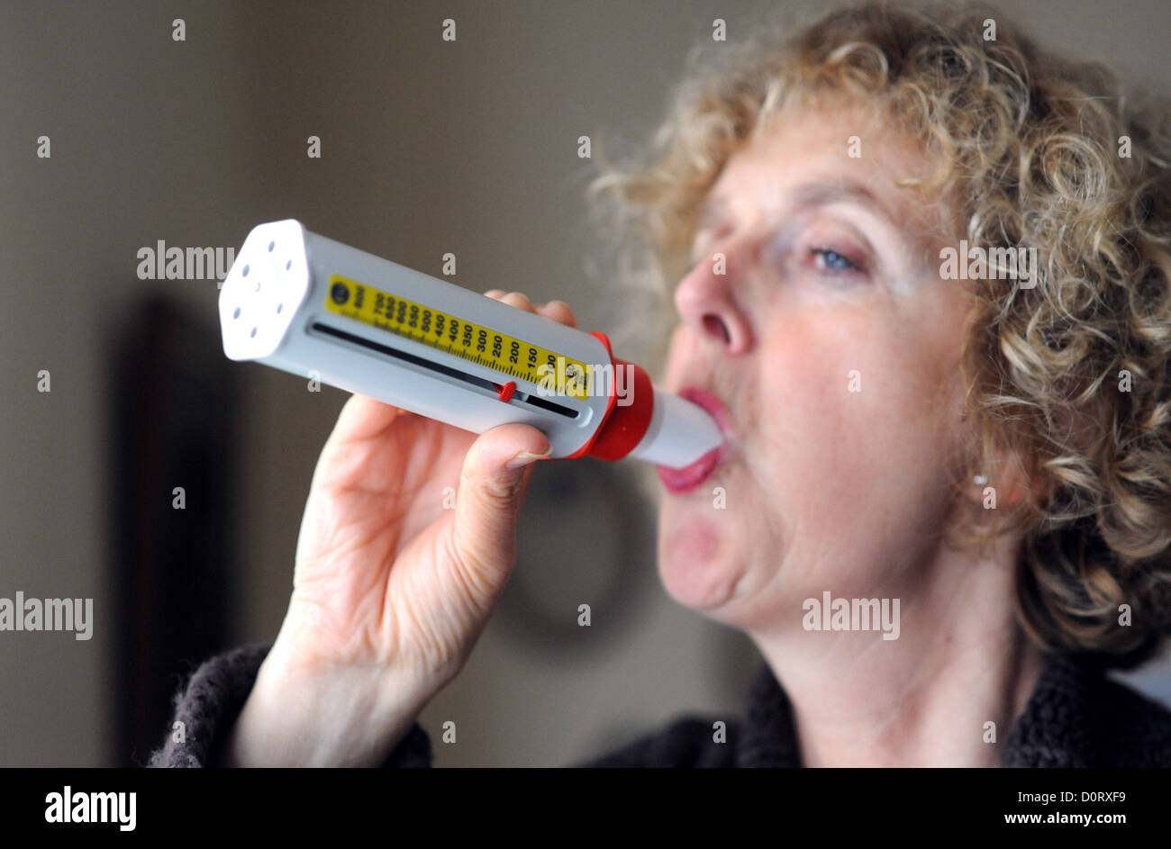 Middle aged female asthma sufferer blowing into a peak flow meter ...