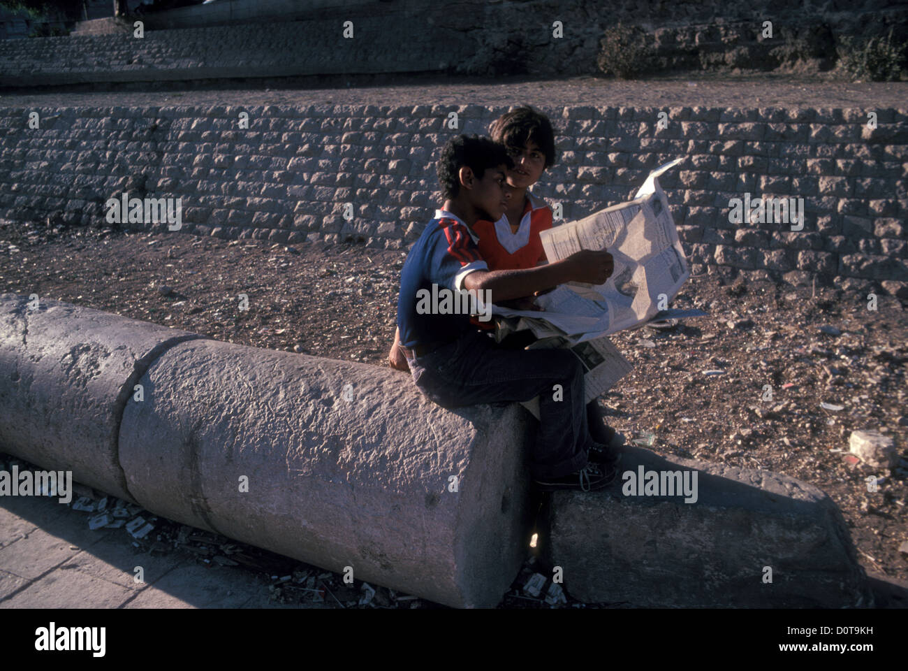 Two young boys read a newspaper on a fallen Roman column in Amman, 1982 ...