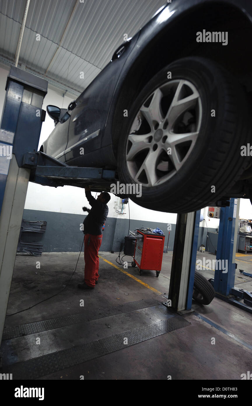 Car mechanic checking a car raised on a hydraulic lift Stock Photo - Alamy