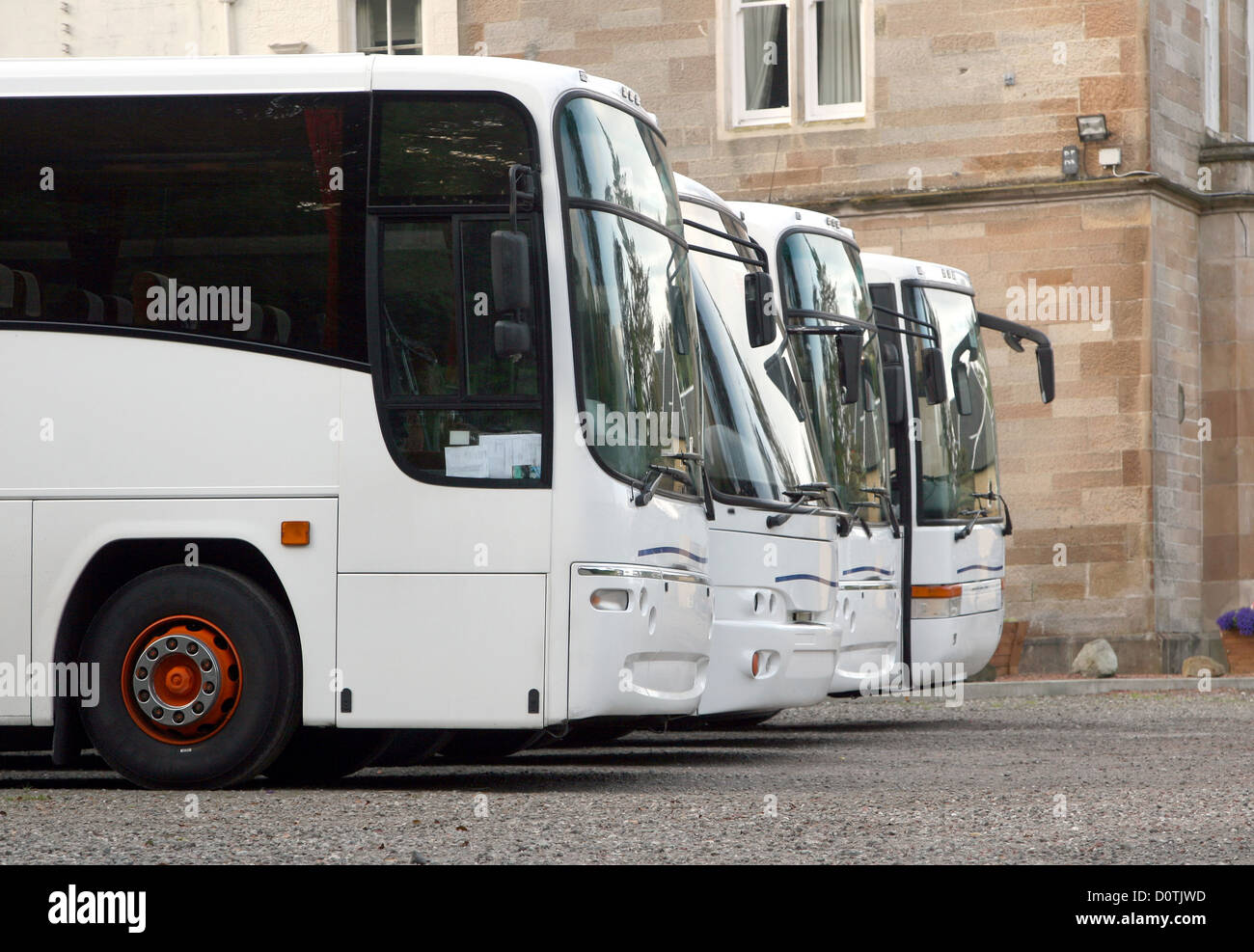 Line of four pure white coaches beside a traditional built stone Hotel ...