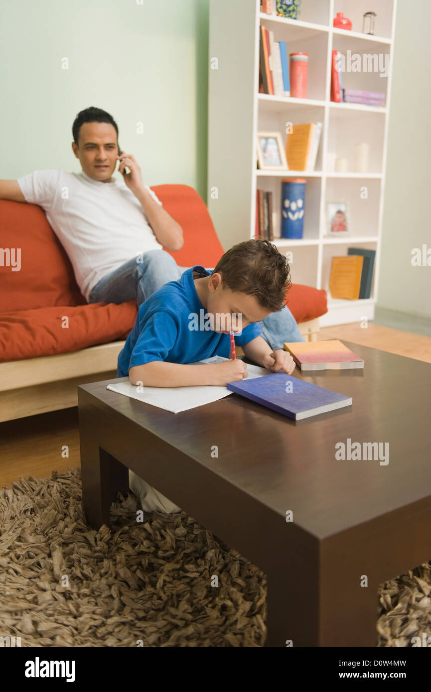 Boy doing homework with father talking on a mobile phone behind him ...