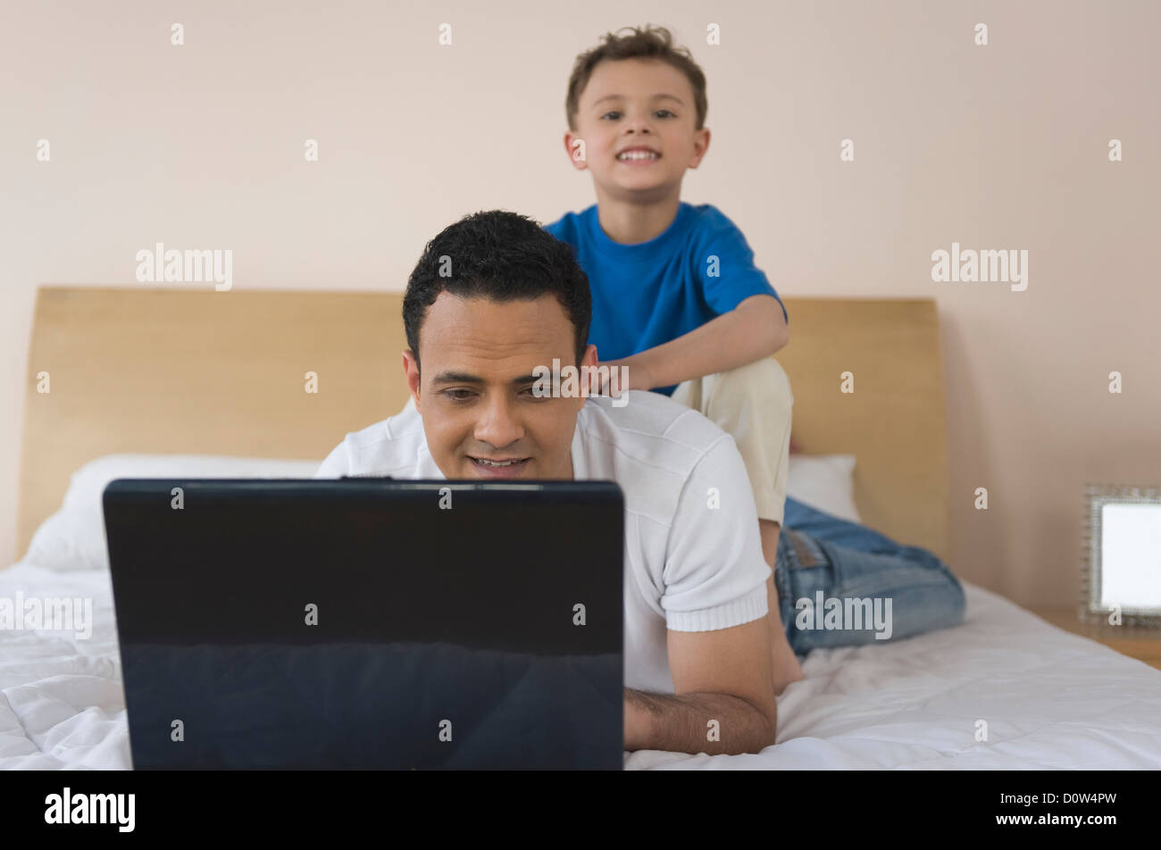 Man using a laptop with son sitting on his back Stock Photo - Alamy