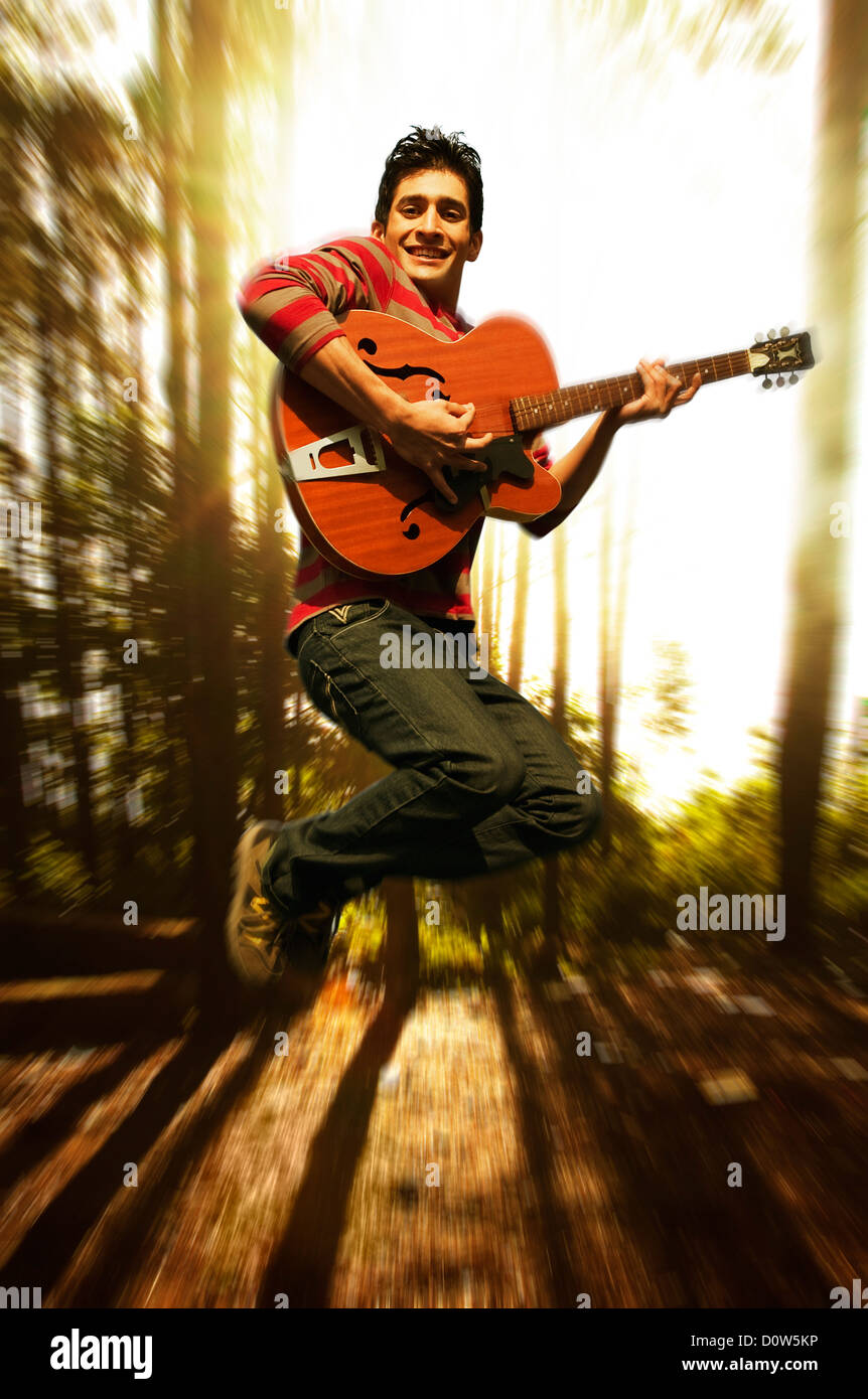 Man playing a guitar and jumping in a forest, Gurgaon, Haryana, India ...