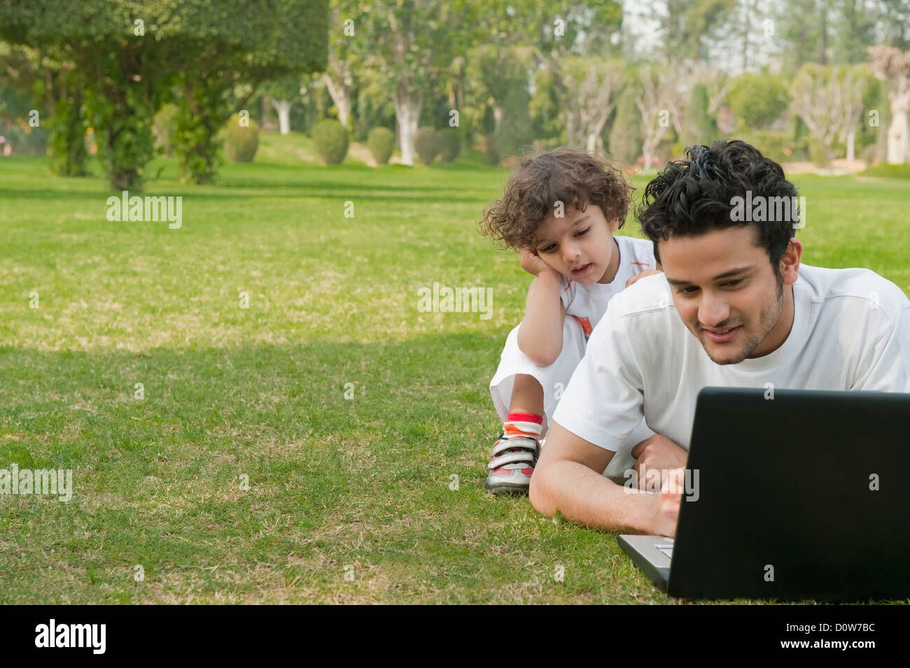 Man working on a laptop while his son sitting beside him Stock Photo ...