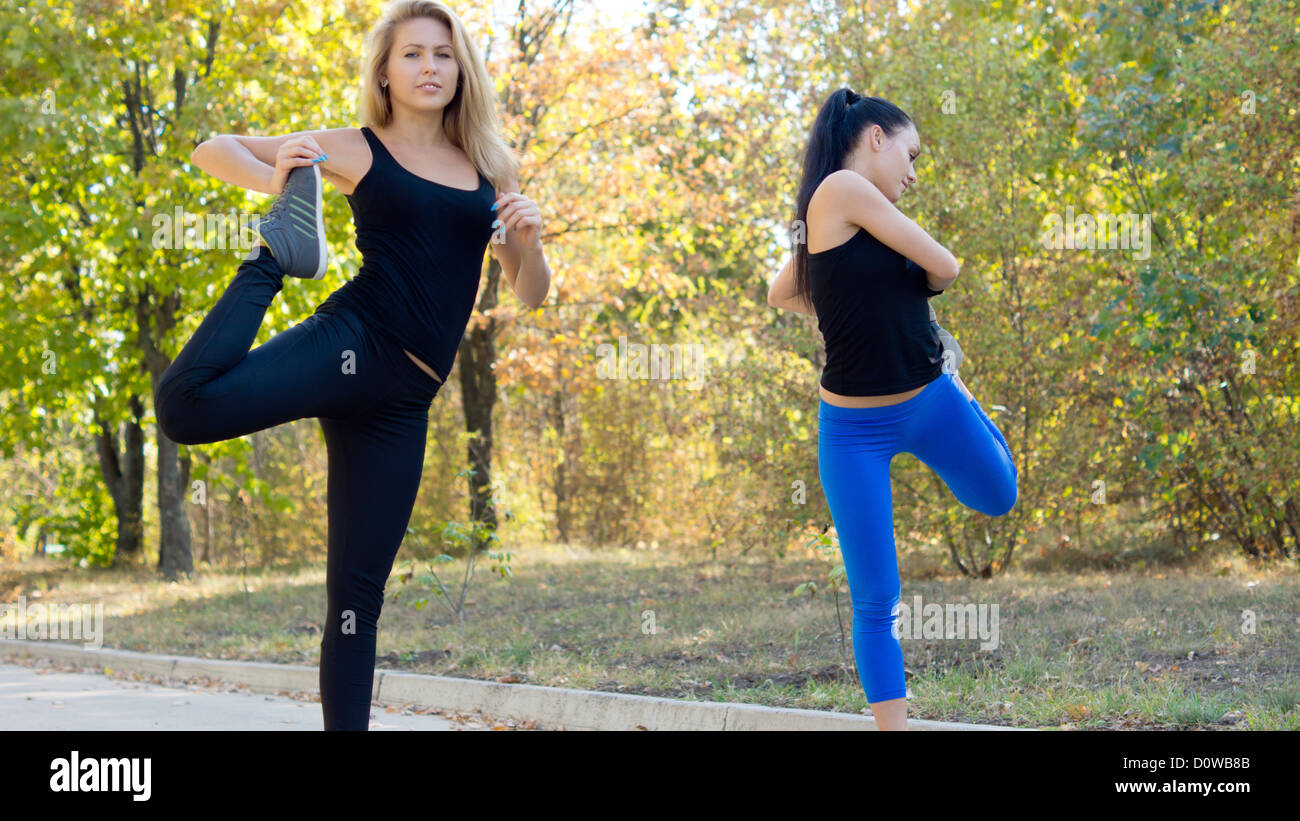 Two women exercising together outdoors in a park stretching and ...