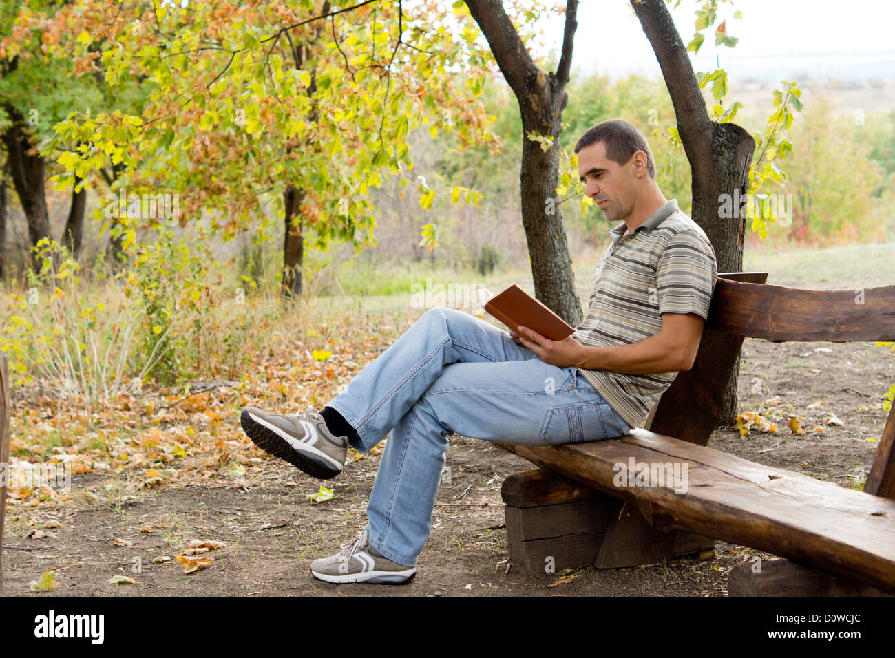Man sitting on a rustic wooden bench relaxing reading a book in the ...