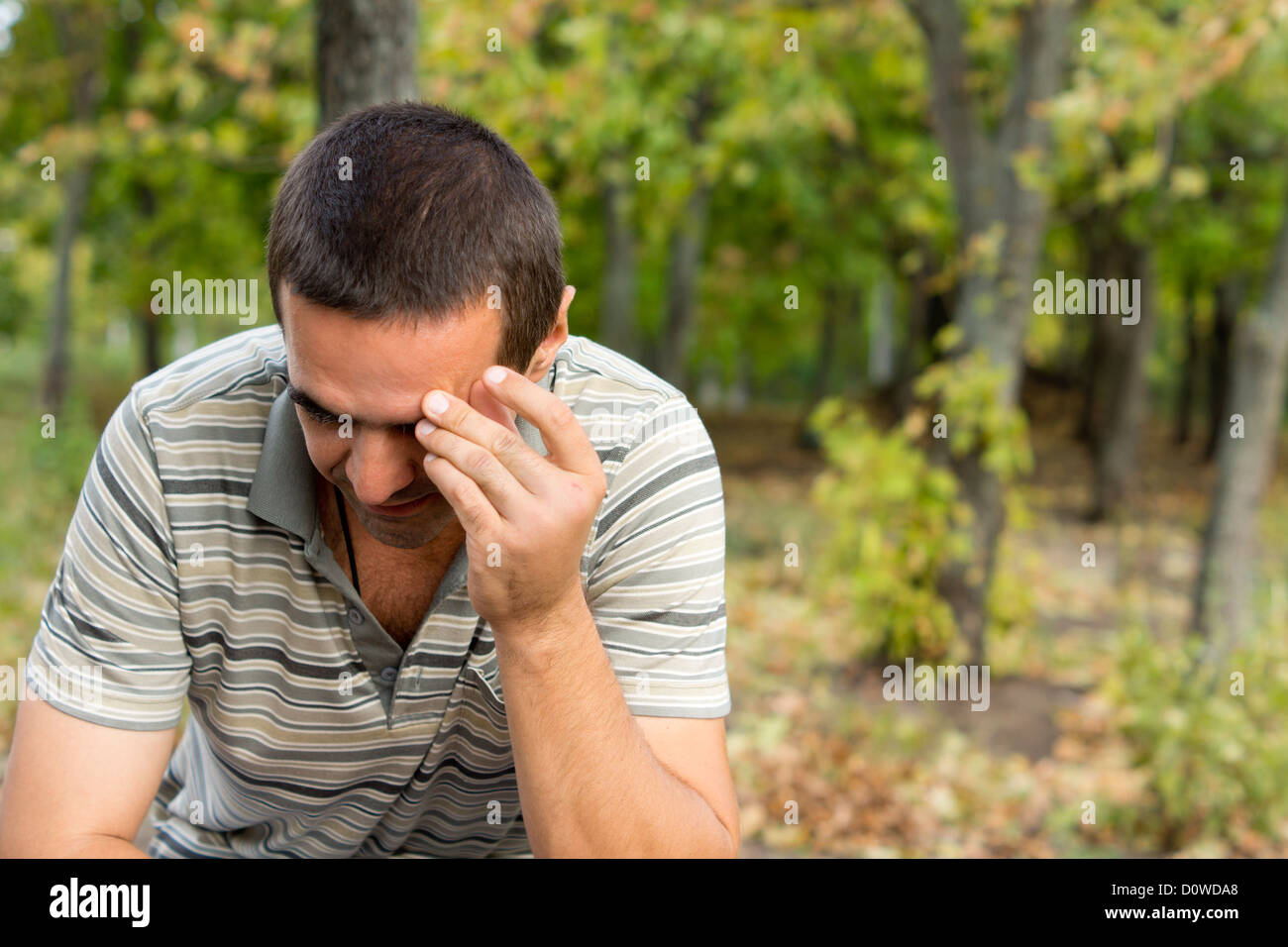 Worried man sitting alone outdoors with his hand raise to his forehead ...