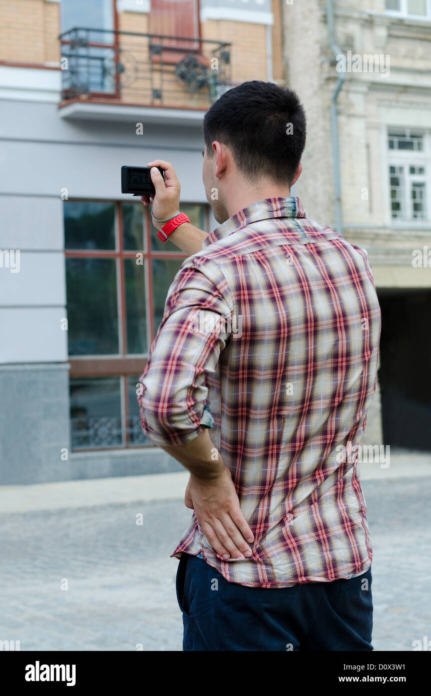 Back view of a young man photographing a building with a small compact ...
