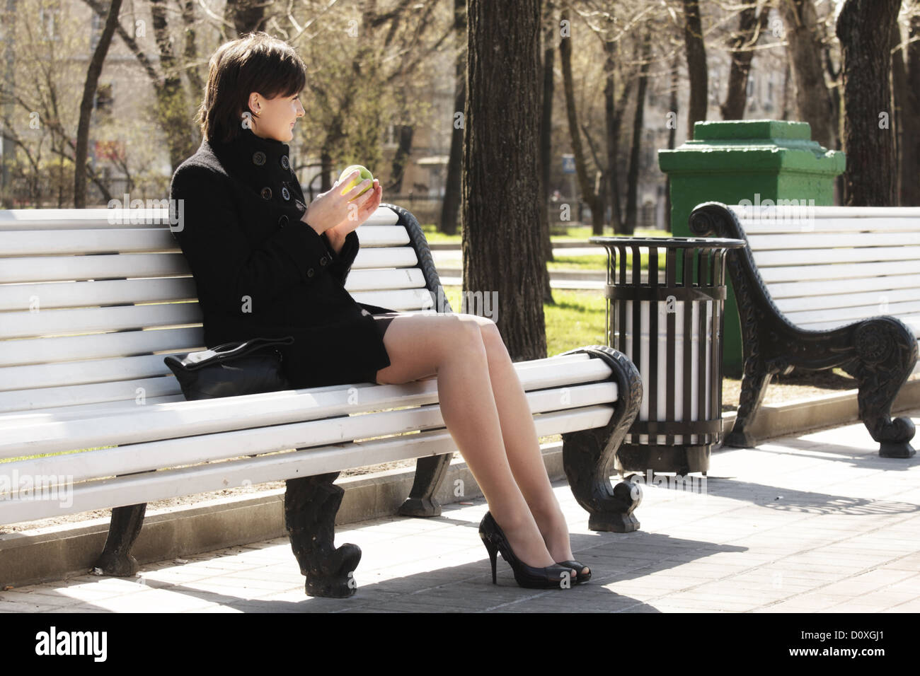 Woman in black with apple on bench Stock Photo - Alamy