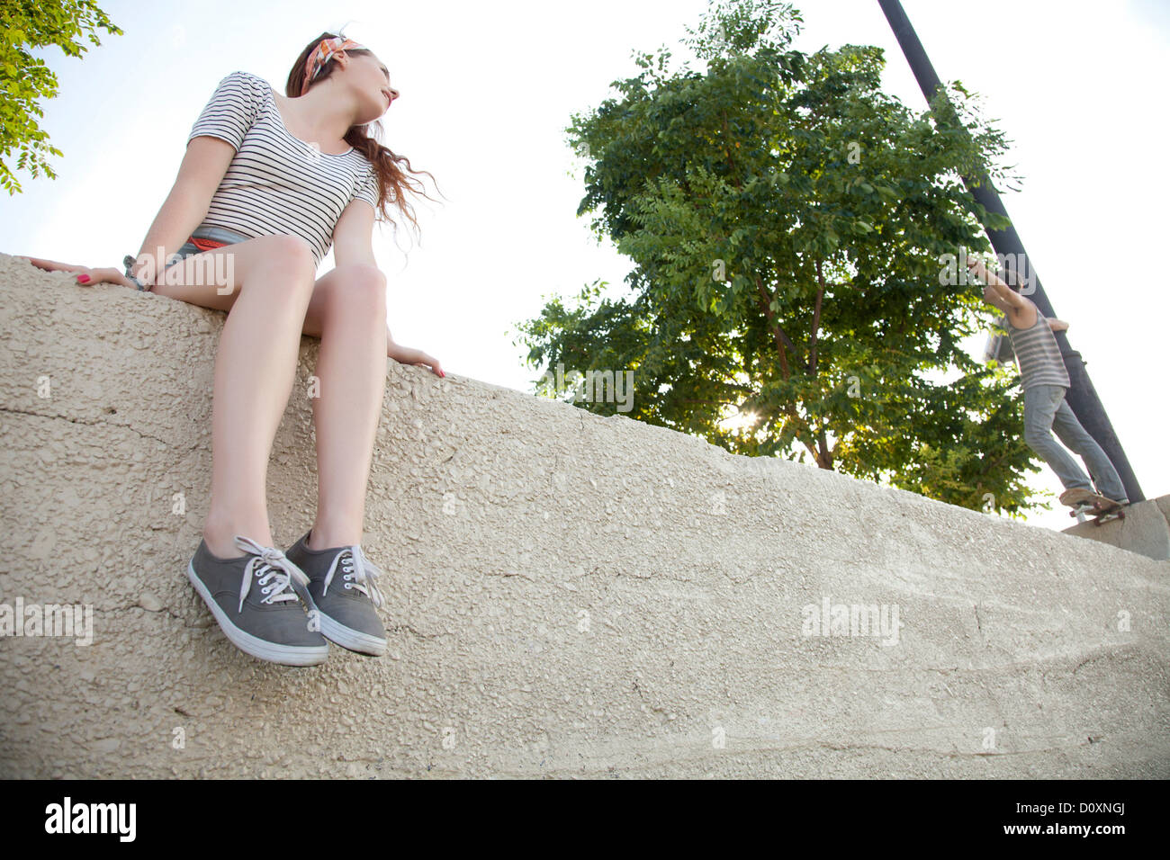 Young woman sitting on wall watching skateboarder Stock Photo - Alamy