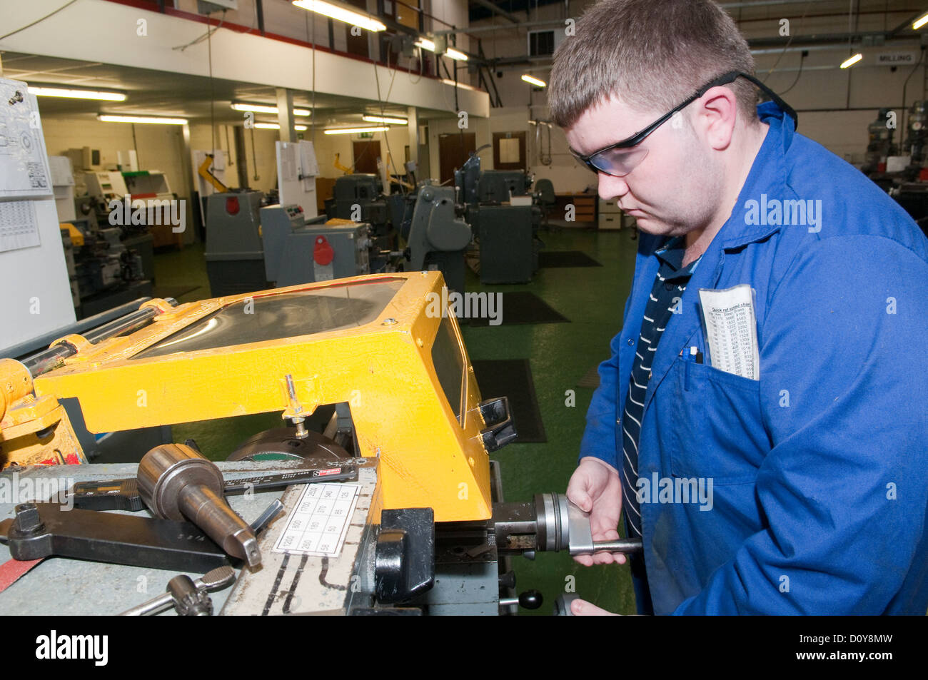 Young white man in blue overalls on a factory floor on an engineering ...