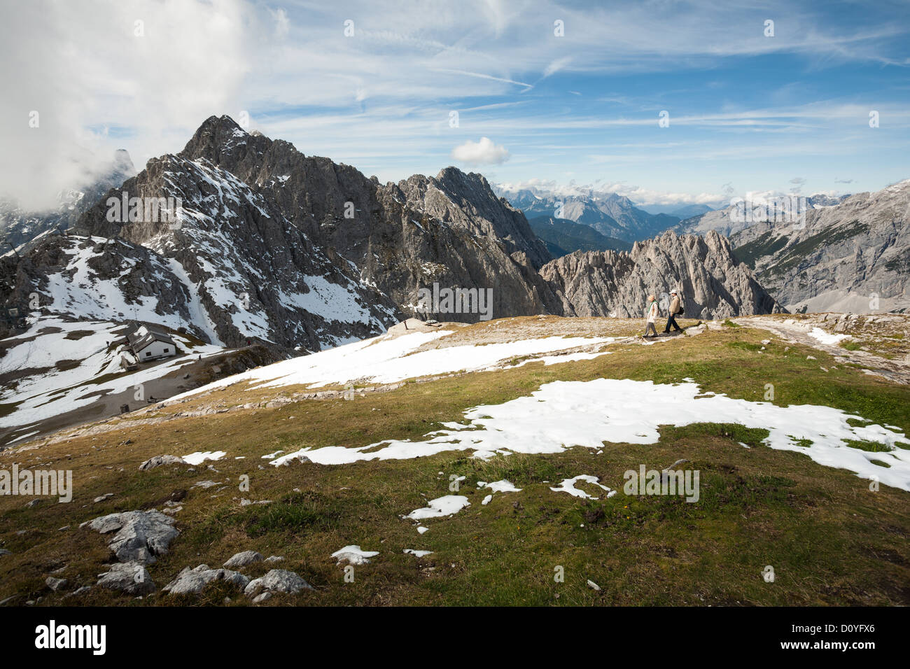 Tourist couple walk across grassy plateau with light snow in Austrian ...