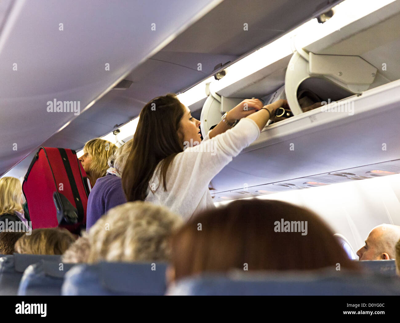 Woman putting luggage into overhead lockers on aircraft, UK Stock Photo ...