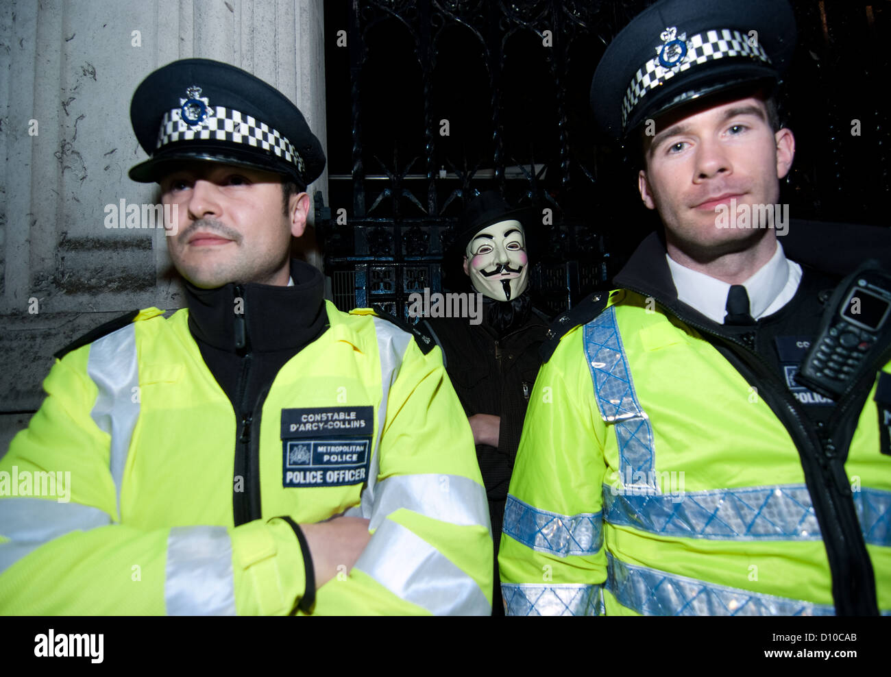 A 'Anonymous' protester stands behind police constables outside the ...