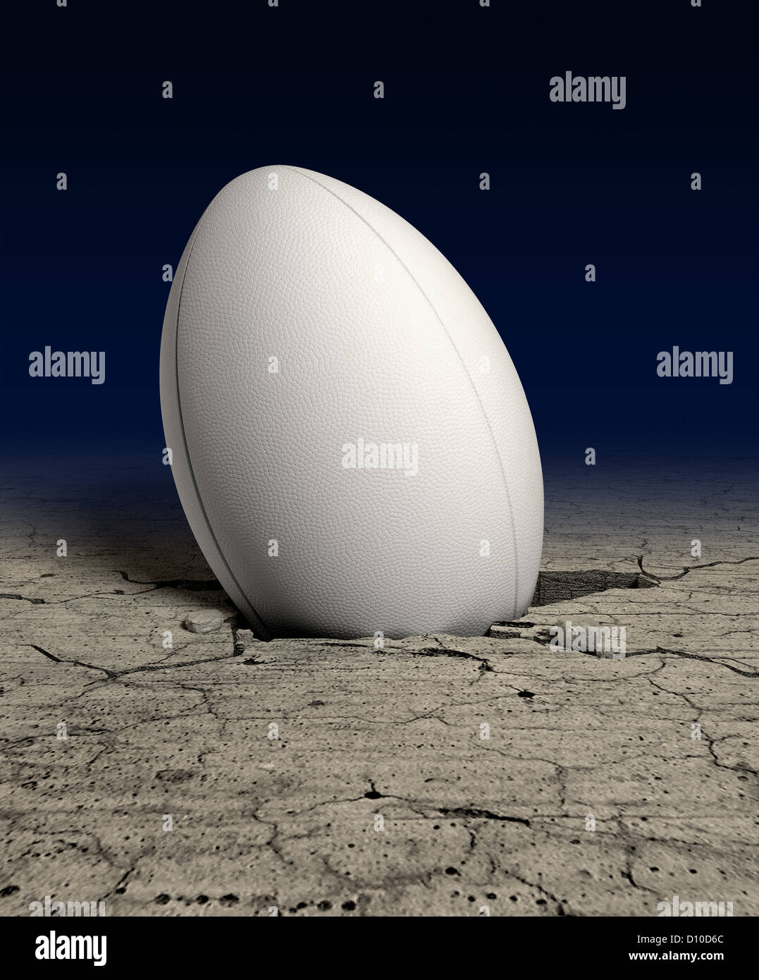 A white dimpled rugby ball stuck in a whole cracked in the ground on a ...