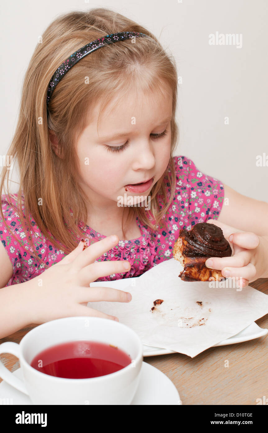 Indoor photo of a little girl with cup of fruit tea eating piece of ...
