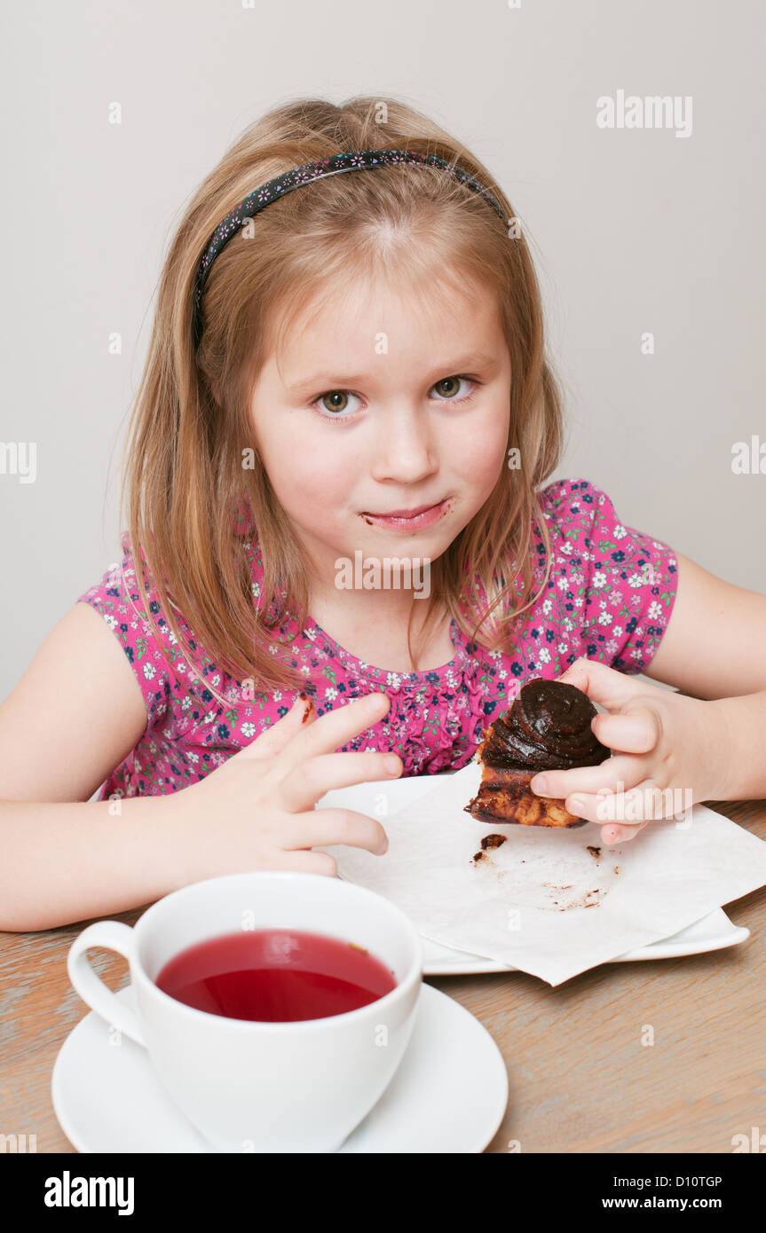 Indoor photo of a little girl with cup of fruit tea eating piece of ...