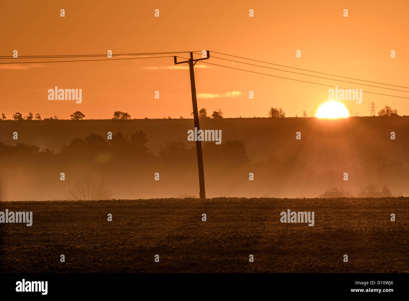 Sunrise over a distant hill with mist rising from the near ground. A ...