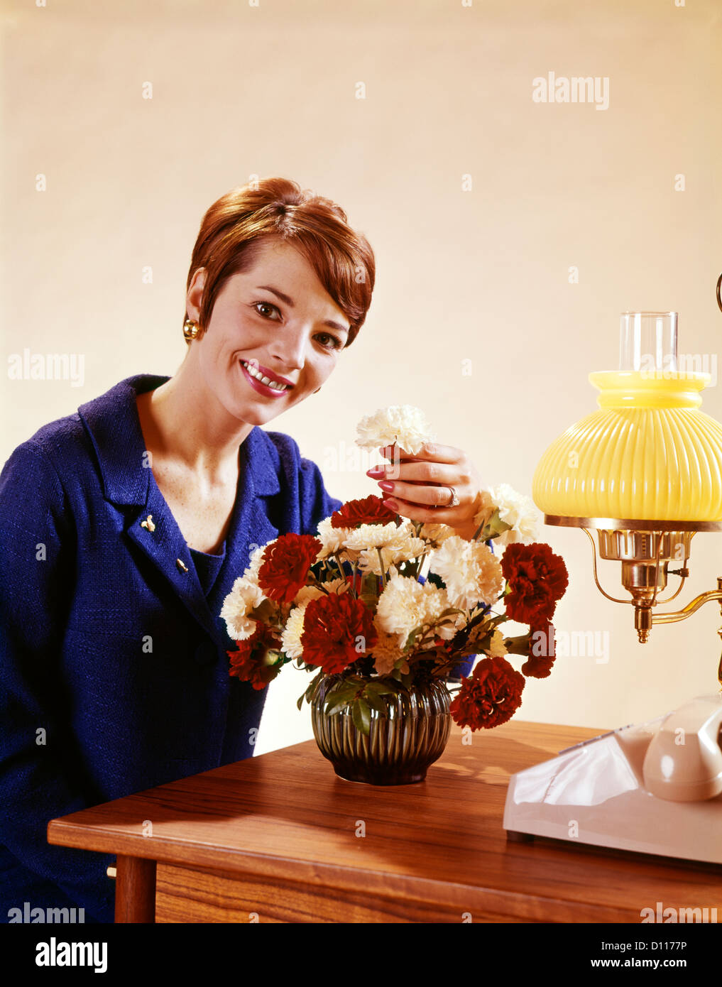 1960s SMILING WOMAN ARRANGING VASE RED WHITE CARNATIONS LOOKING AT ...
