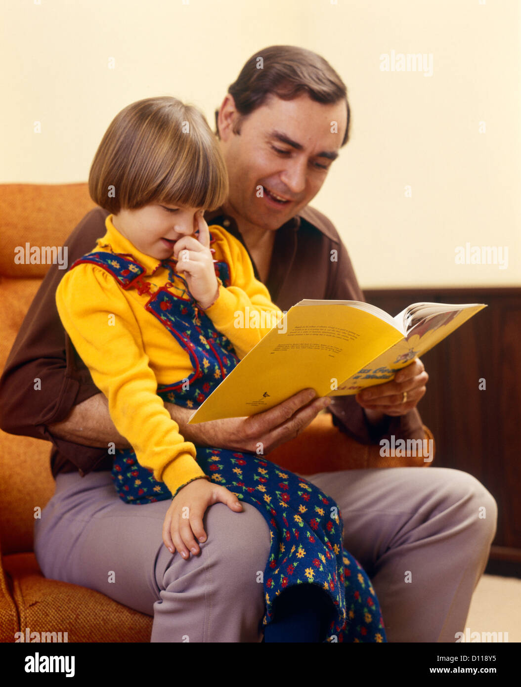 1970s FATHER READING BOOK TO DAUGHTER SITTING ON LAP Stock Photo - Alamy