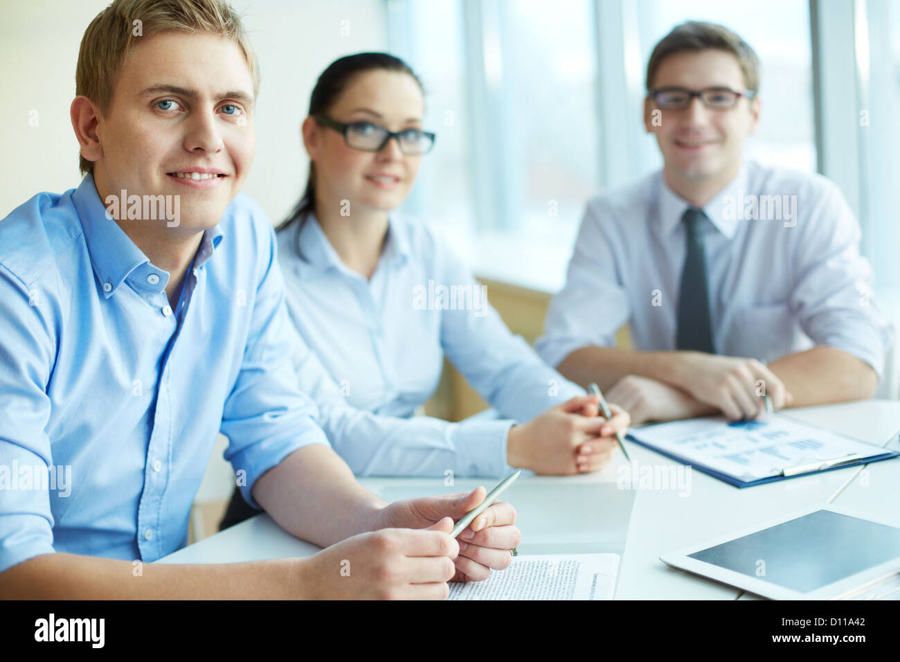 Image of handsome leader looking at camera with two employees behind ...
