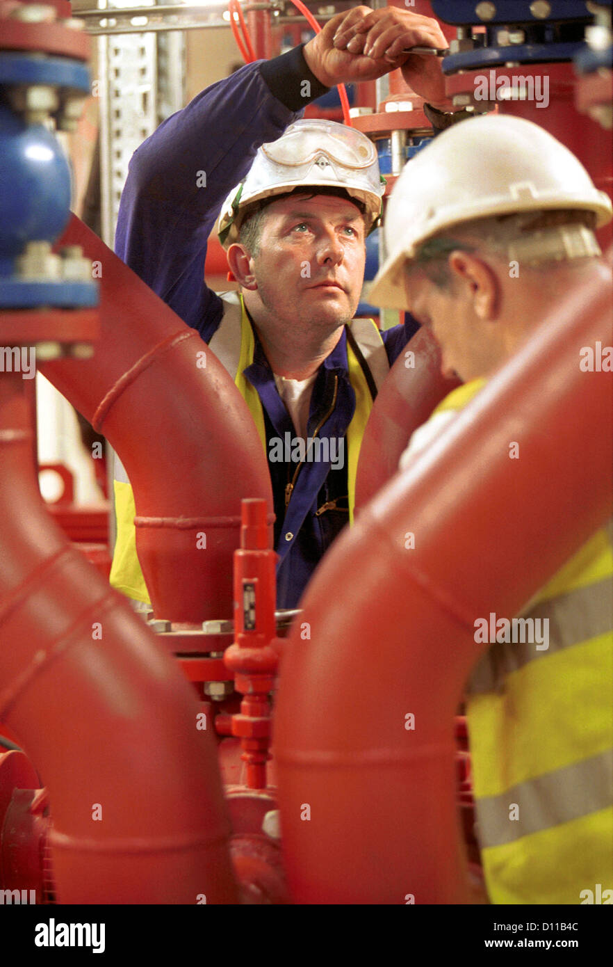 Two workers working as a team Tightening valves using a spanner Stock ...