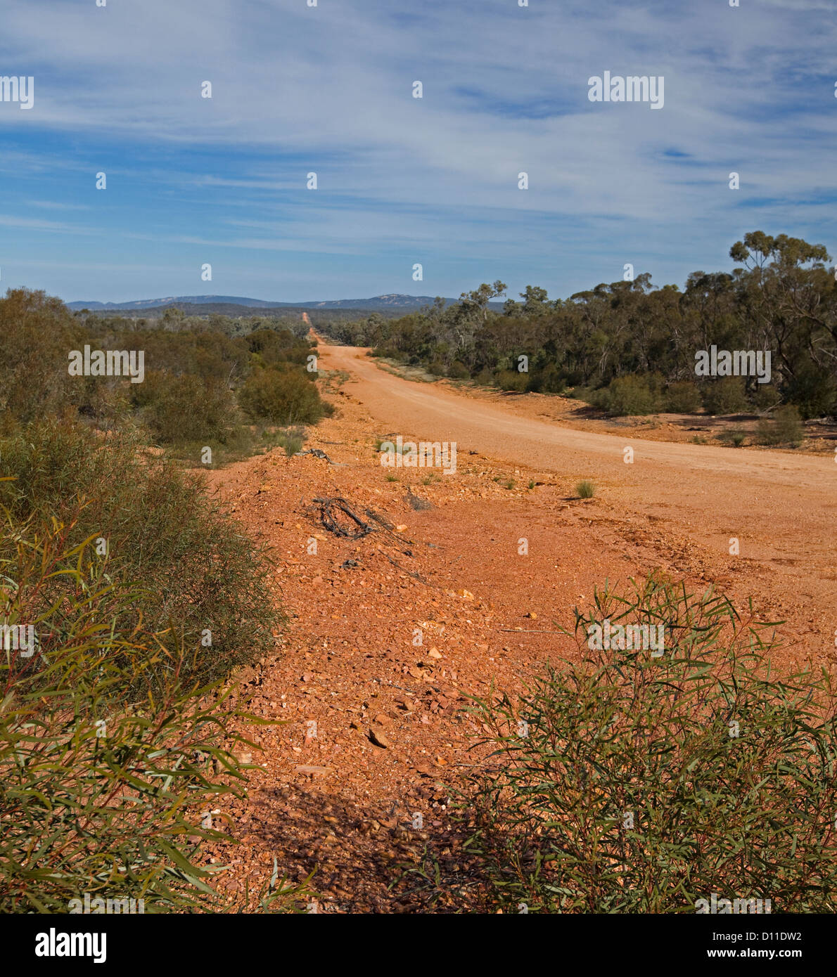 Long straight Australian outback road through low woodlands to distant ...