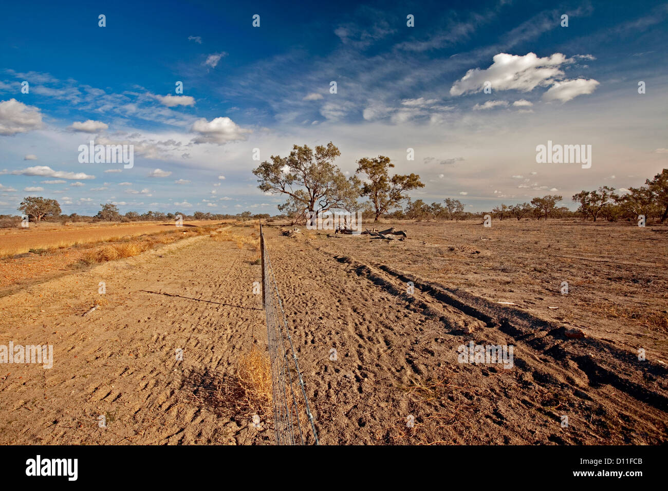 Vast arid Australian outback landscape with dusty dirt road, fence, and ...