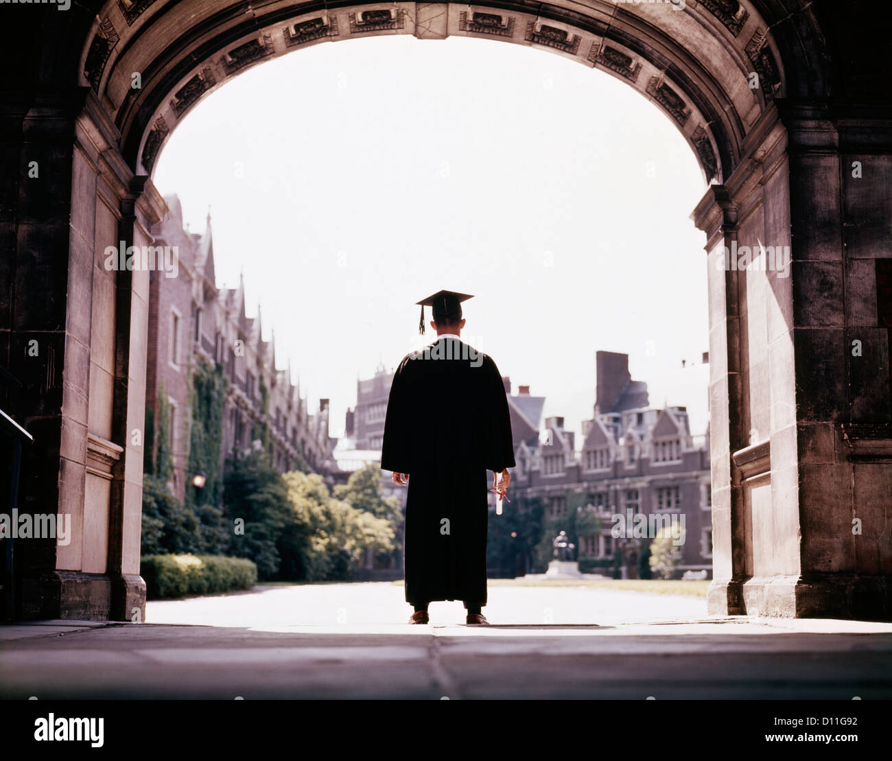 1960s 1960s BACK VIEW MALE GRADUATE WEARING CAP GOWN STANDING IN CAMPUS ...