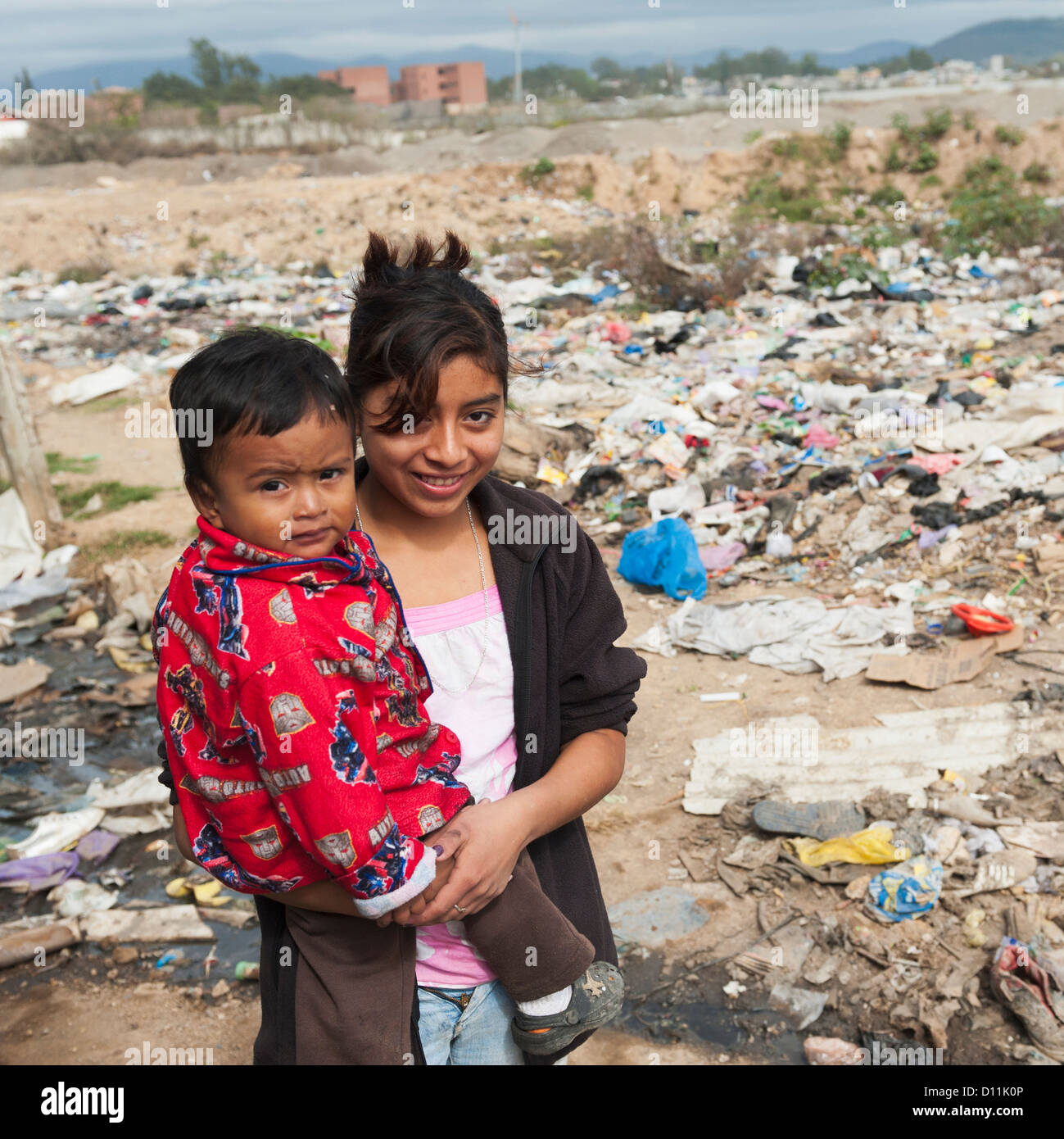 A Girl Holds Her Young Brother While Standing In A Garbage Dump ...