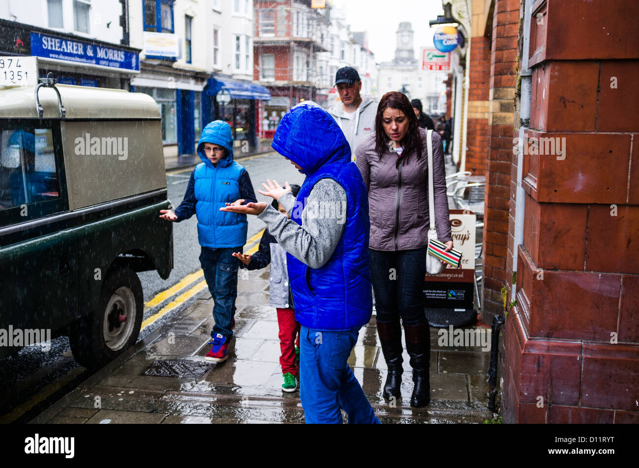 A family walking in the rain in a town centre street, Aberystwyth Wales ...