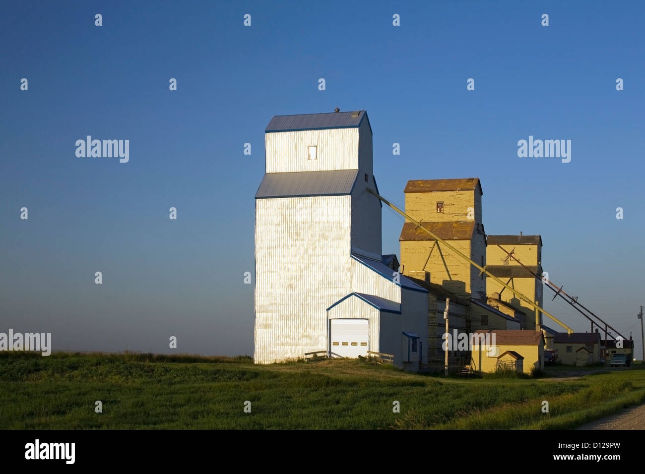 A Row Of Grain Elevators At Sunrise With Blue Sky; Mossleigh Alberta ...