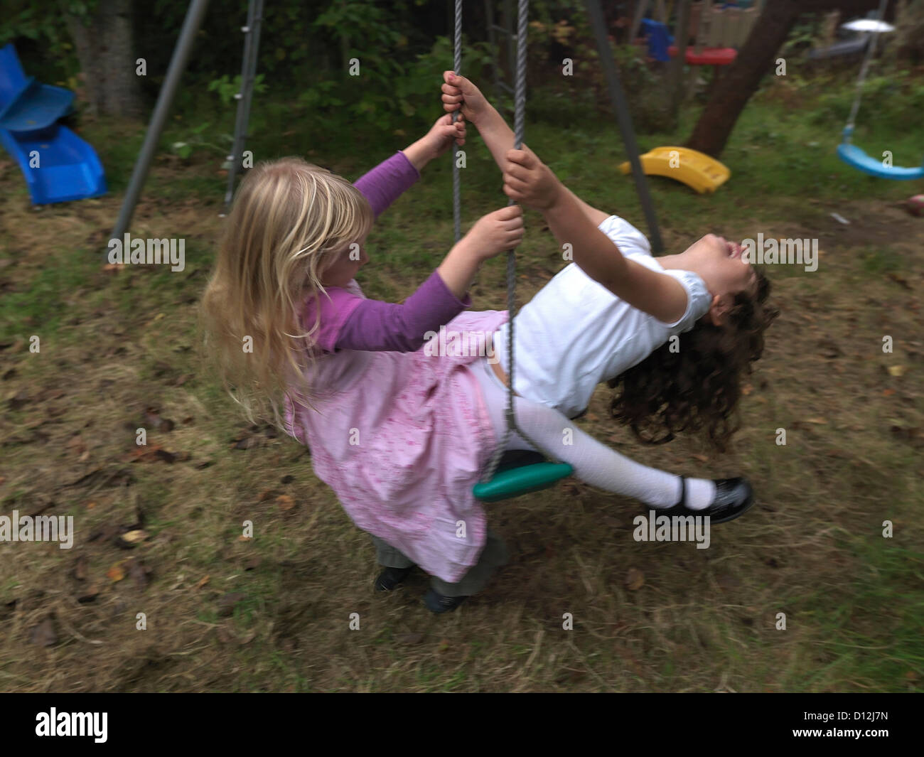 Sisters Sitting On Swing Together In Garden England Stock Photo - Alamy