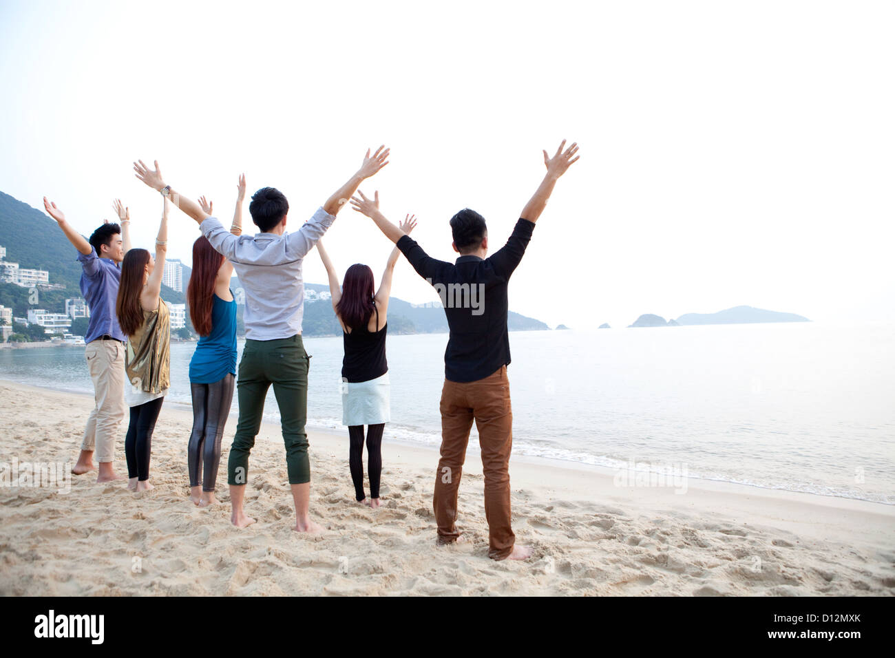 Rear view of happy young people raising hands on the beach of Repulse ...