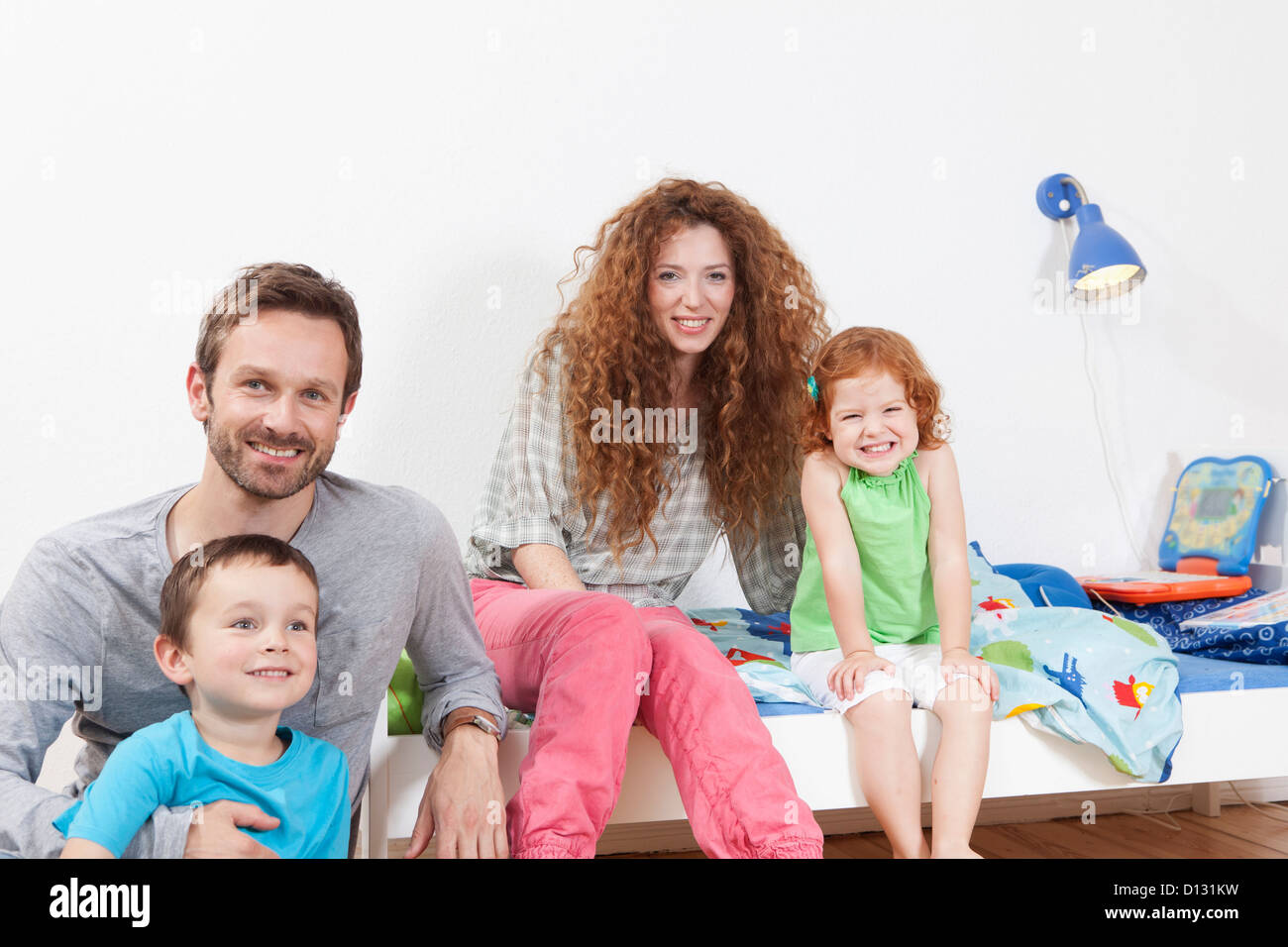 Germany, Berlin, Family sitting on bed, smiling, portrait Stock Photo ...