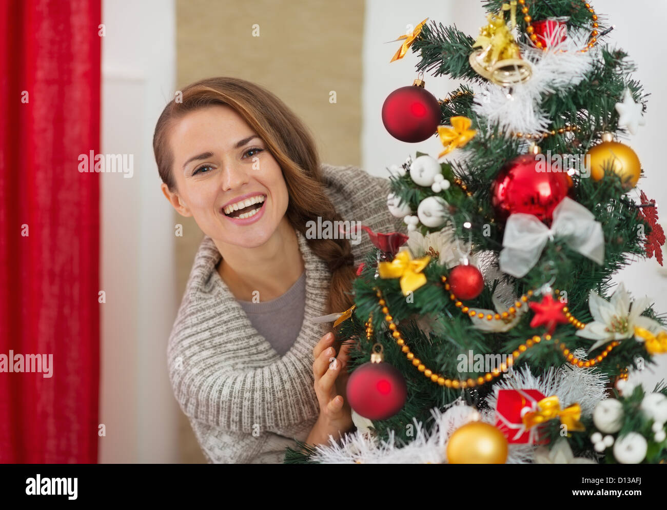 Happy young woman looking out from Christmas tree Stock Photo - Alamy