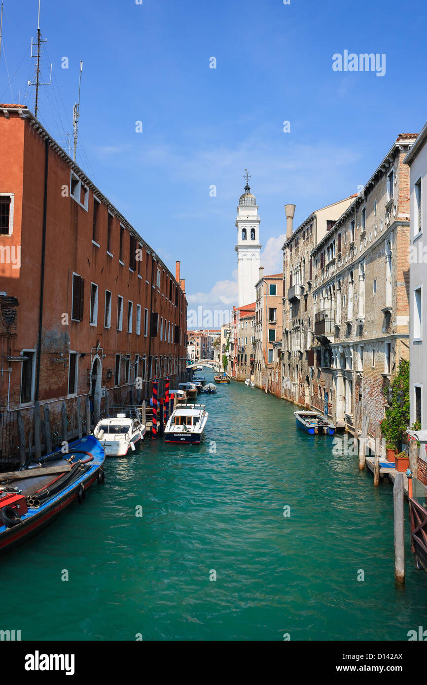 A church tower at the end of a small narrow sub canal full of boats in ...