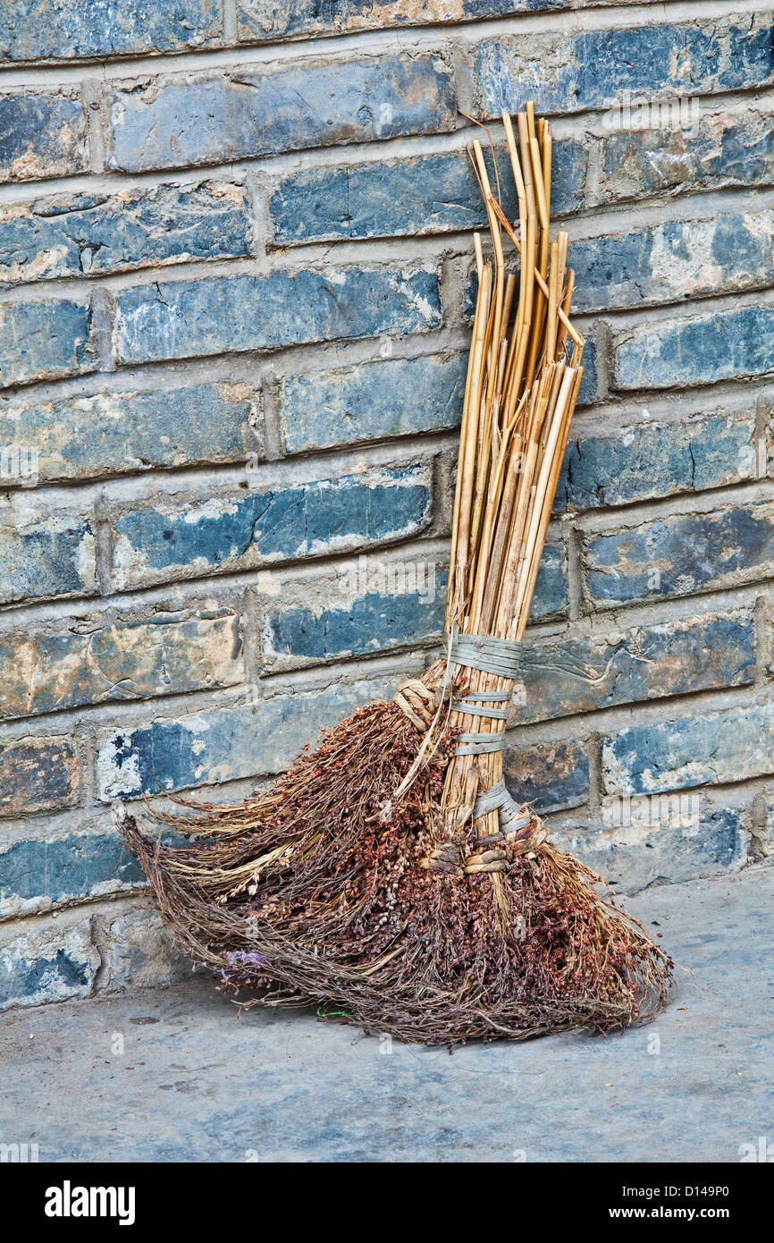 Home made broom laying against a brick wall in the Ancient town of Daxu ...