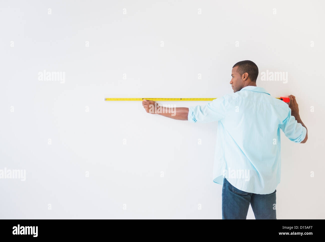 Young man measuring white wall Stock Photo - Alamy