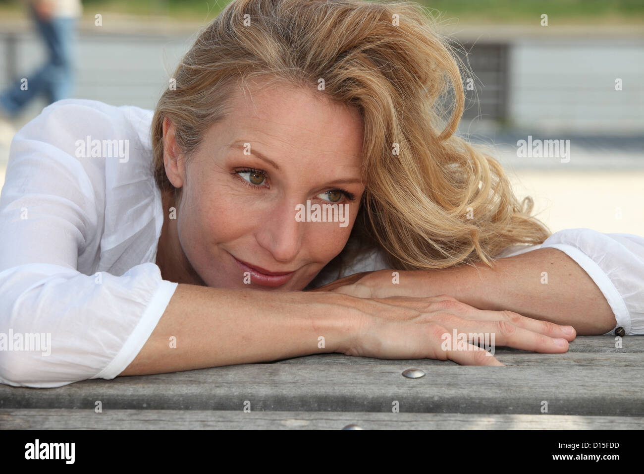 Woman with long blonde hair leaning on a bench Stock Photo - Alamy