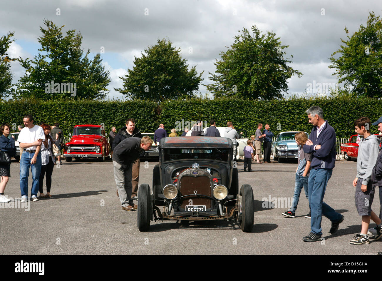 A crowd of people at a car show looking at a hotrod car parked on ...