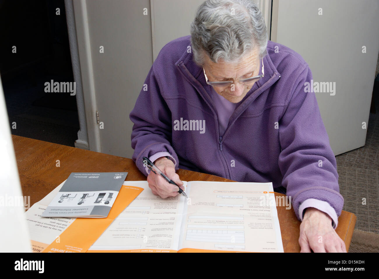 Elderly woman filling in an application form to claim for benefits ...
