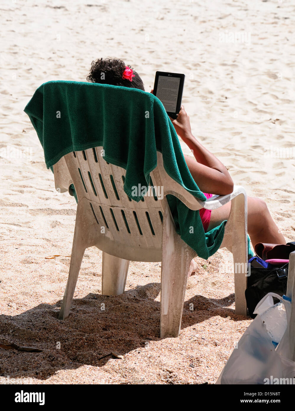 woman sitting deck chair white sandy beach read reading book on tablet ...