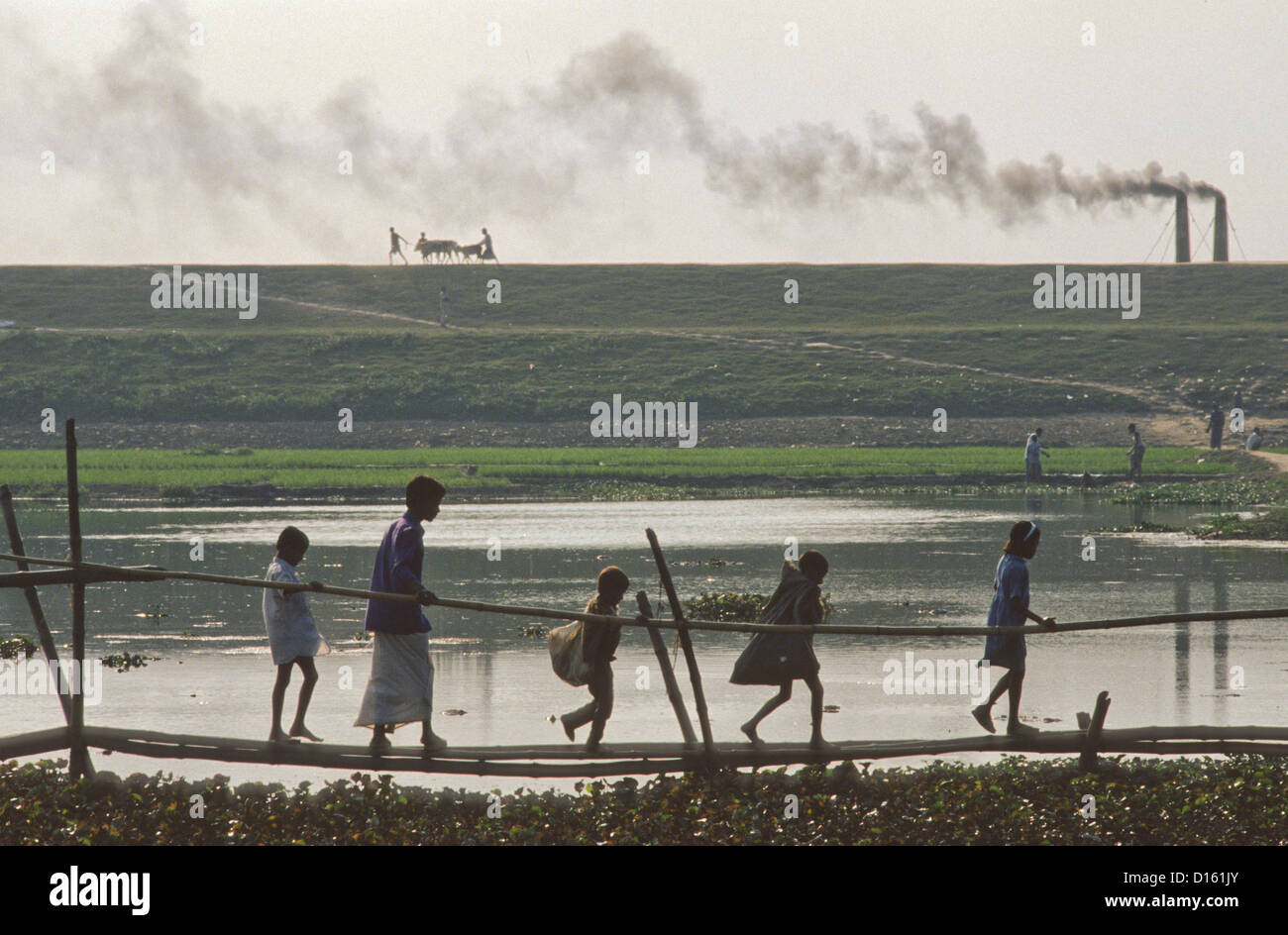 Family walking by flooded canal in the slums of Dhaka, with factory ...