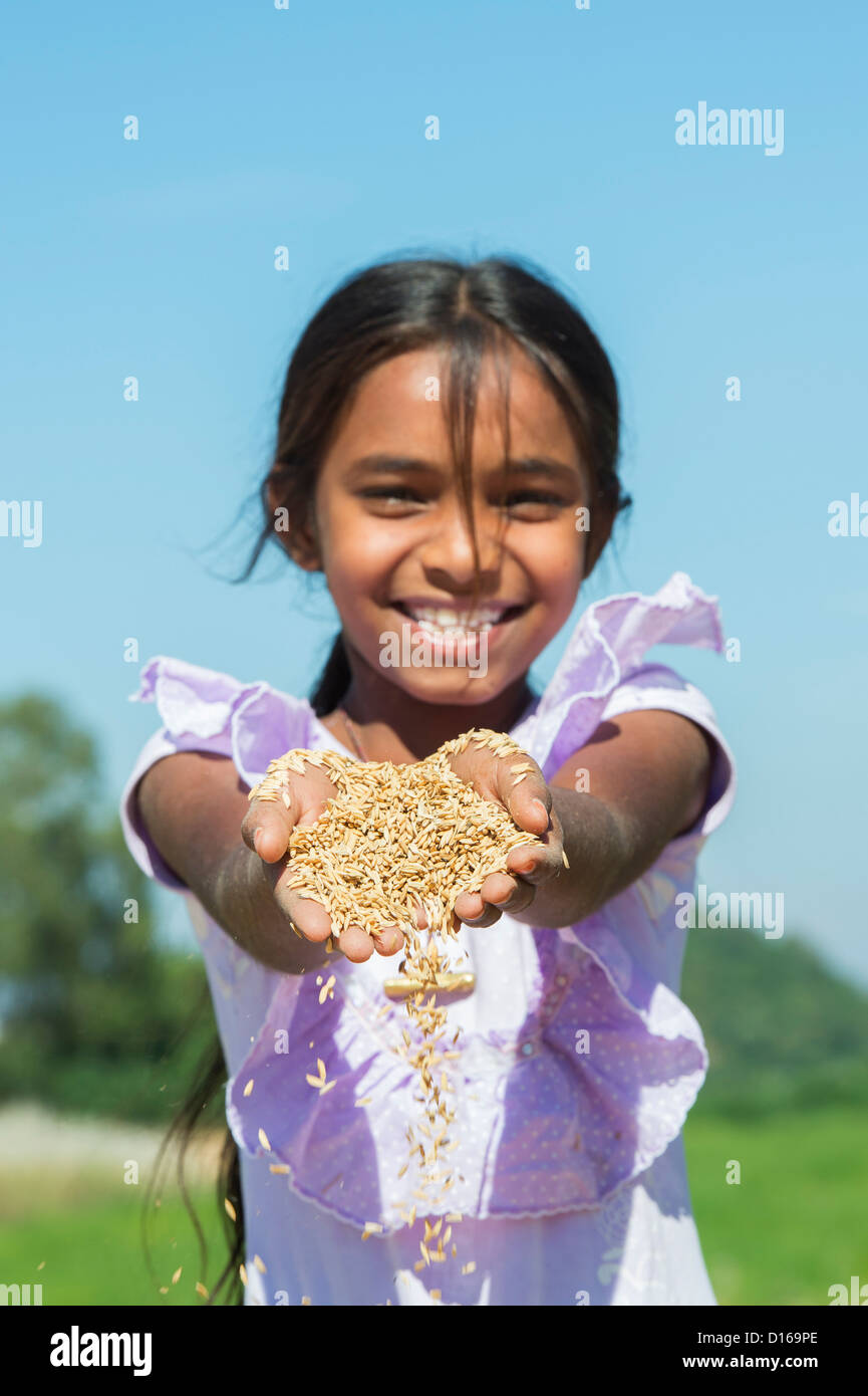 Happy smiling rural Indian girl holding harvested rice grains her hands ...
