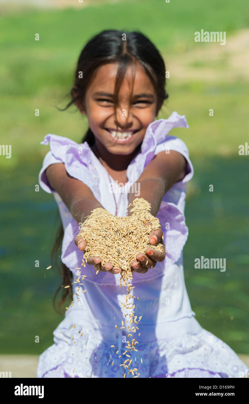 Happy smiling rural Indian girl holding harvested rice grains her hands ...