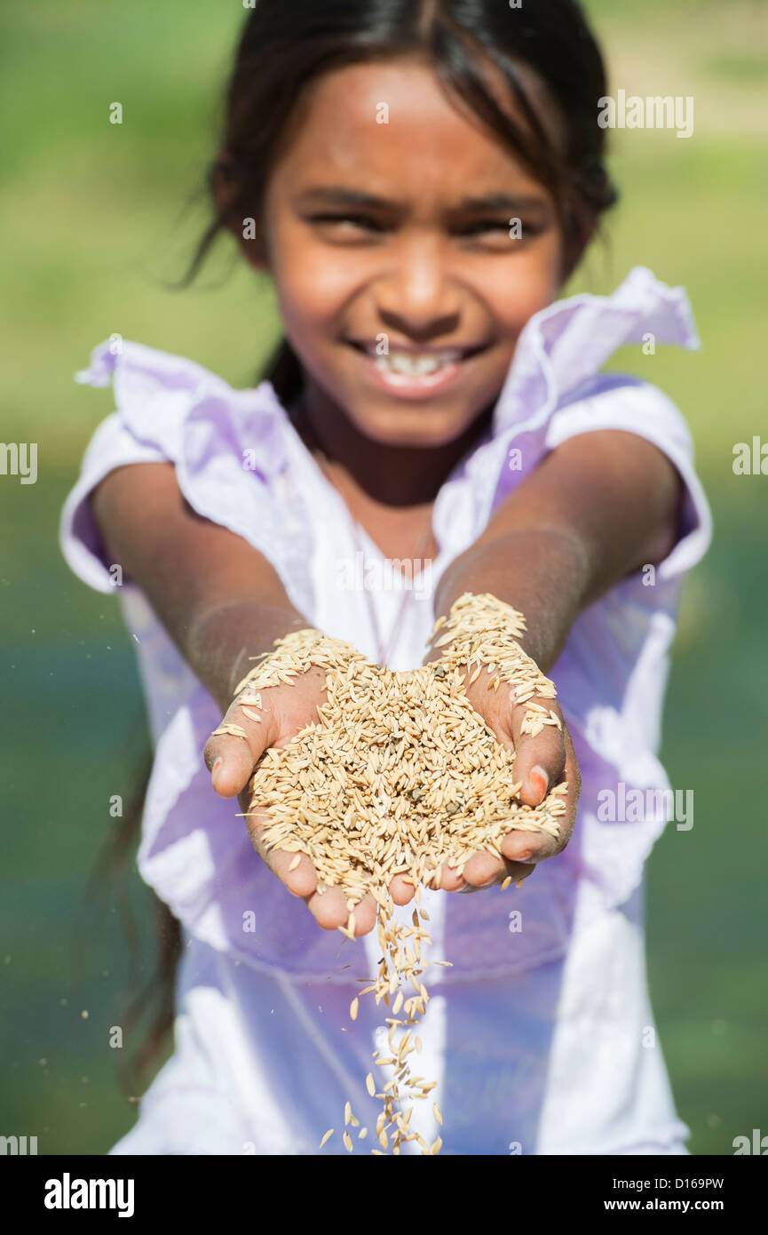 Happy smiling rural Indian girl holding harvested rice grains her hands ...